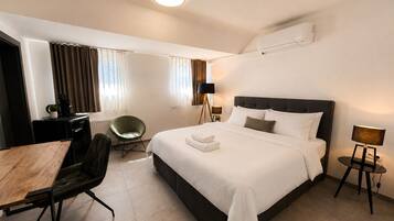 Quarto de hotel com cama, escrivaninha, cadeira, abajur e aparelho de ar condicionado.