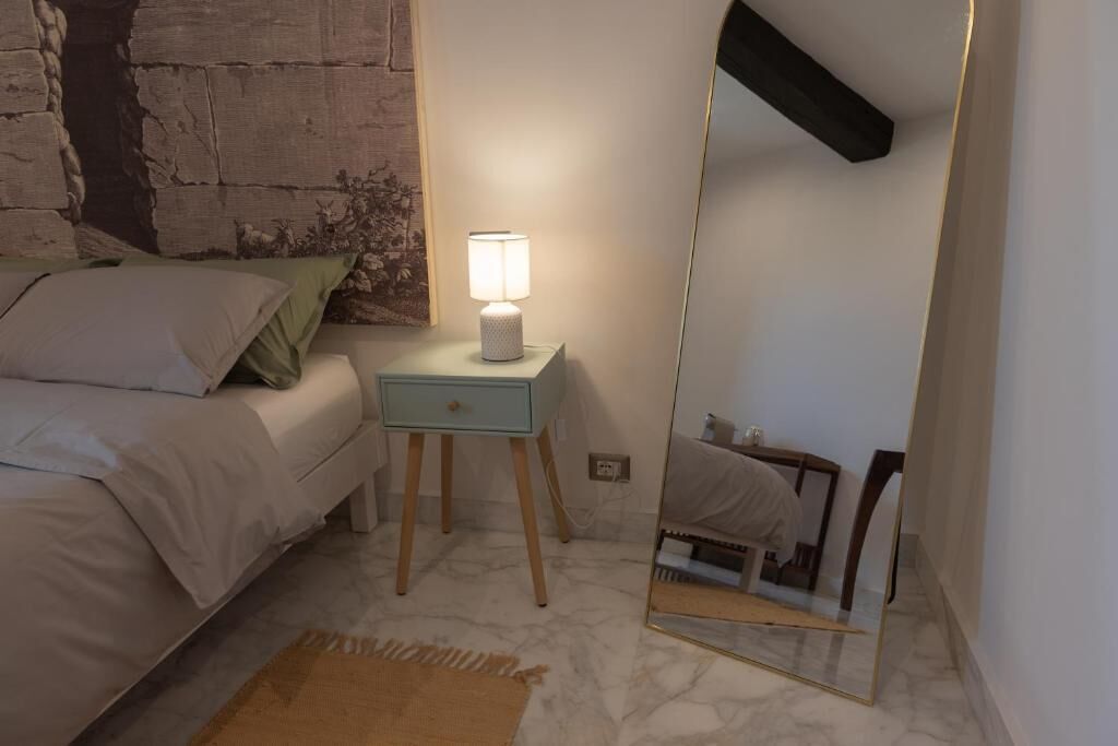 Quarto com cama, mesa de cabeceira com abajur, espelho e parede de pedra.
