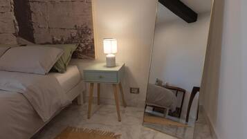 Quarto com cama, mesa de cabeceira com abajur, espelho e parede de pedra.