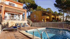 Uma piscina com um deck ladrilhado, espreguiçadeiras e um edifício com varanda.