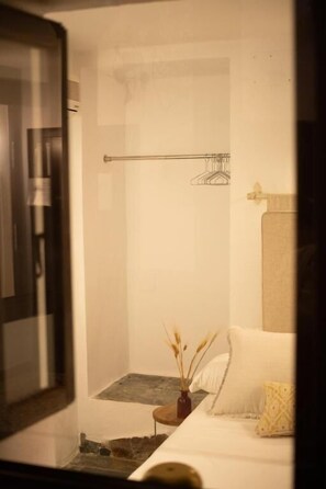 Quarto de hotel com cama, uma pequena mesa com um vaso, um porta-toalhas e área de chuveiro.