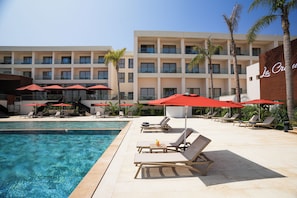 Uma área de piscina de hotel com espreguiçadeiras, guarda-sóis e uma piscina azul cristalina.