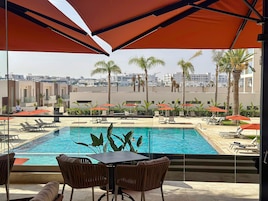 Área à beira da piscina com espreguiçadeiras, guarda-sóis e vista para edifícios ao fundo.