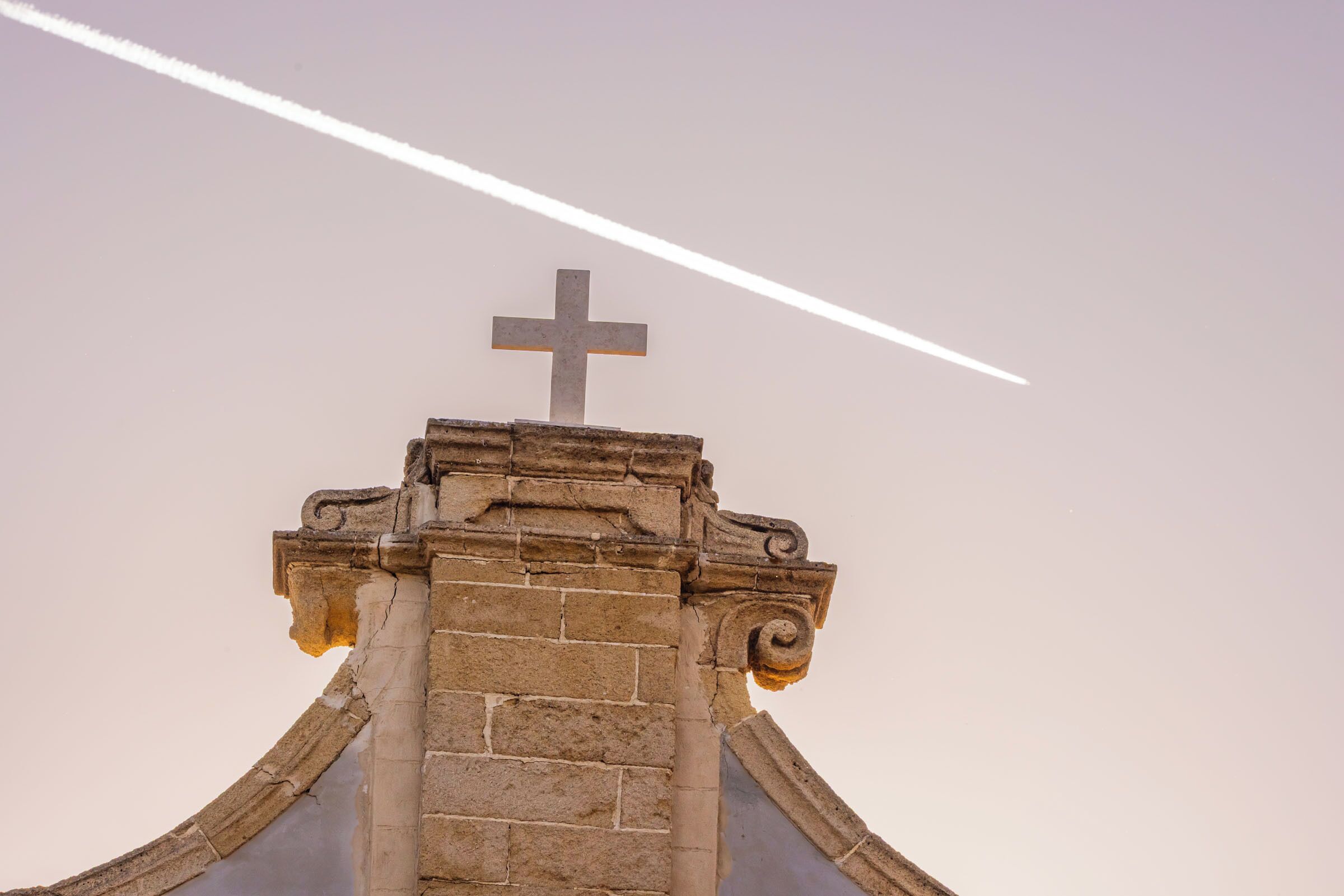 Um pináculo de igreja com uma cruz no topo, estrutura de tijolo e telhado pontiagudo.