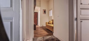 Um corredor com piso de madeira, um sofá amarelo e uma porta à direita.