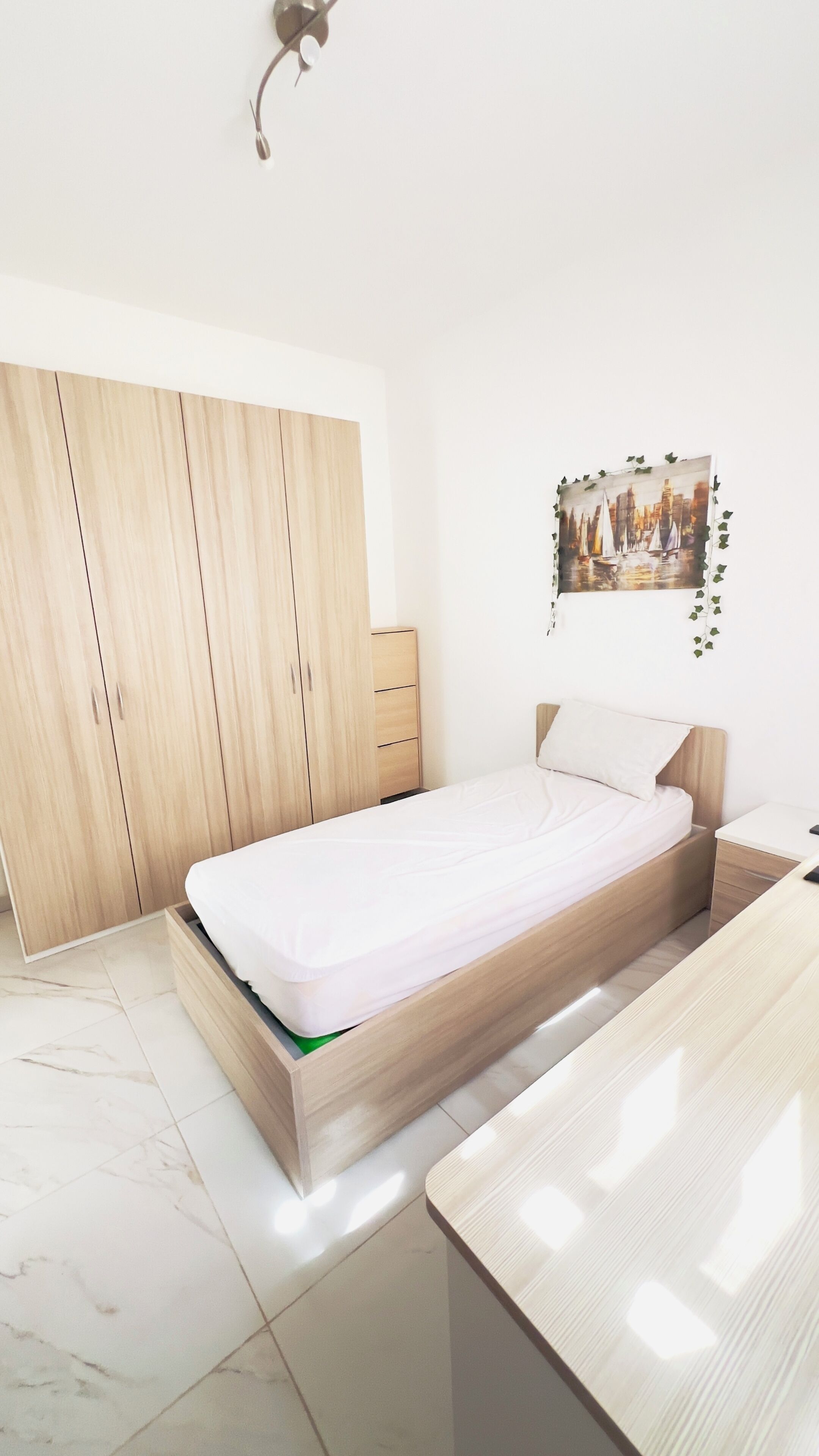 Quarto com cama, guarda-roupa, mesa de cabeceira e um quadro na parede.