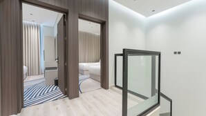 Quarto de hotel moderno com piso de madeira, porta de vidro, cama com tapete listrado e banheiro com cortina.