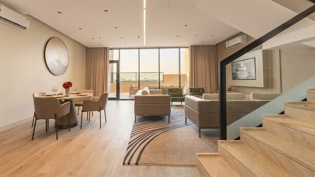 Uma sala de estar moderna com área de jantar, escada e uma grande janela com vista para a cidade.