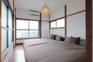 Quarto com duas camas, janelas amplas, luminária pendente e vigas de madeira.