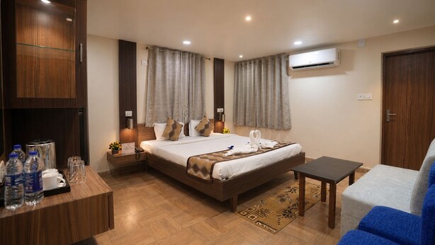 Quarto de hotel com cama, mesa de cabeceira e escrivaninha com garrafas de água.
