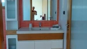 Casa de banho com chão em mosaico vermelho, toucador branco com espelho e zona de duche.