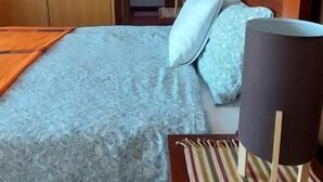 Quarto com uma cama, guarda-roupa de madeira, espelho e mesa de cabeceira com abajur.