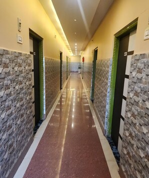 Um corredor de hotel com piso polido, paredes com padrão de pedra e portas verdes.