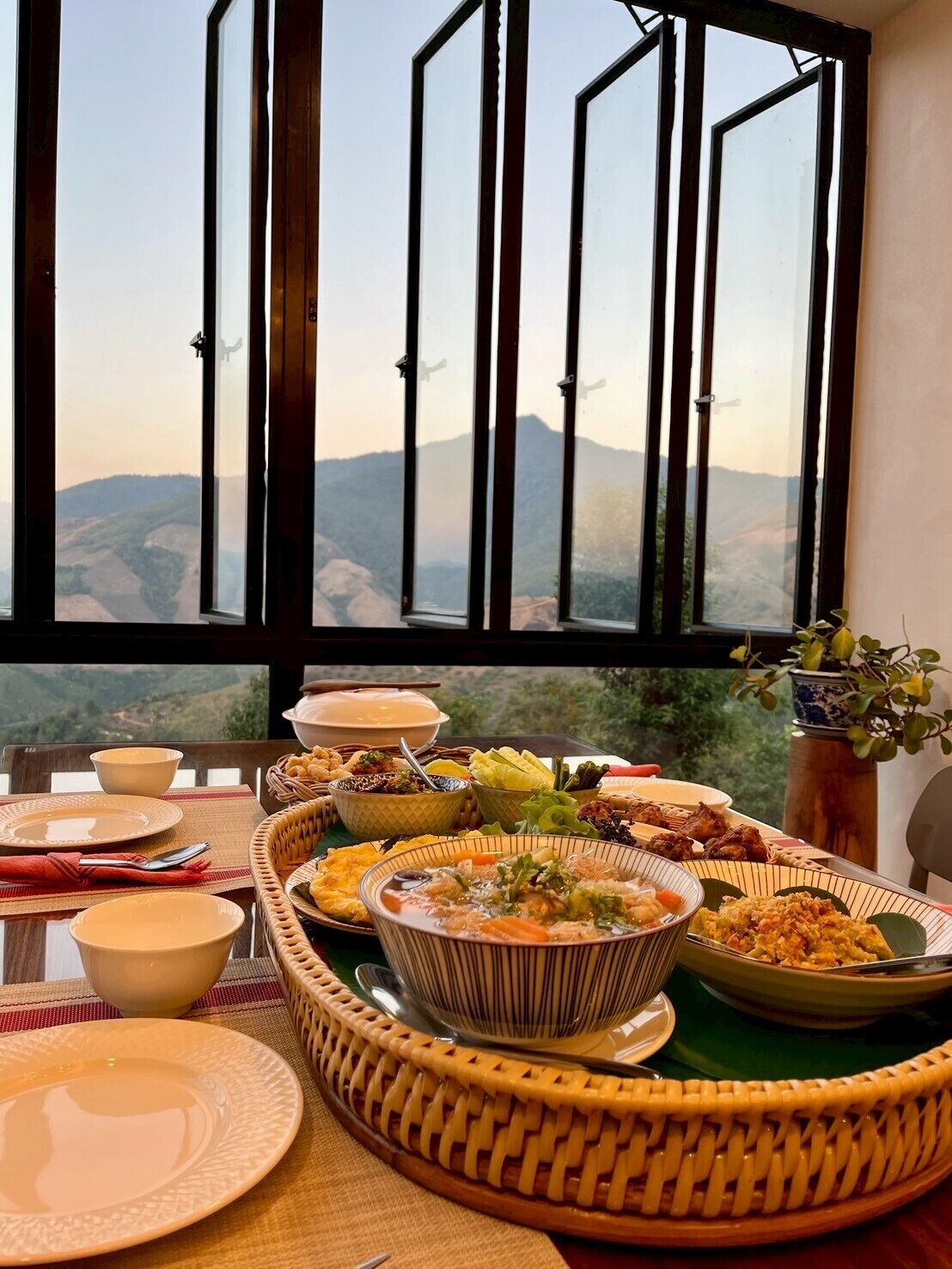 Mesa de jantar com vários pratos e vista para montanhas através de grandes janelas.