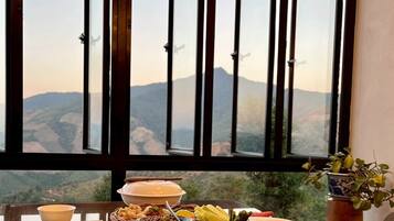 Mesa de jantar com vários pratos e vista para montanhas através de grandes janelas.