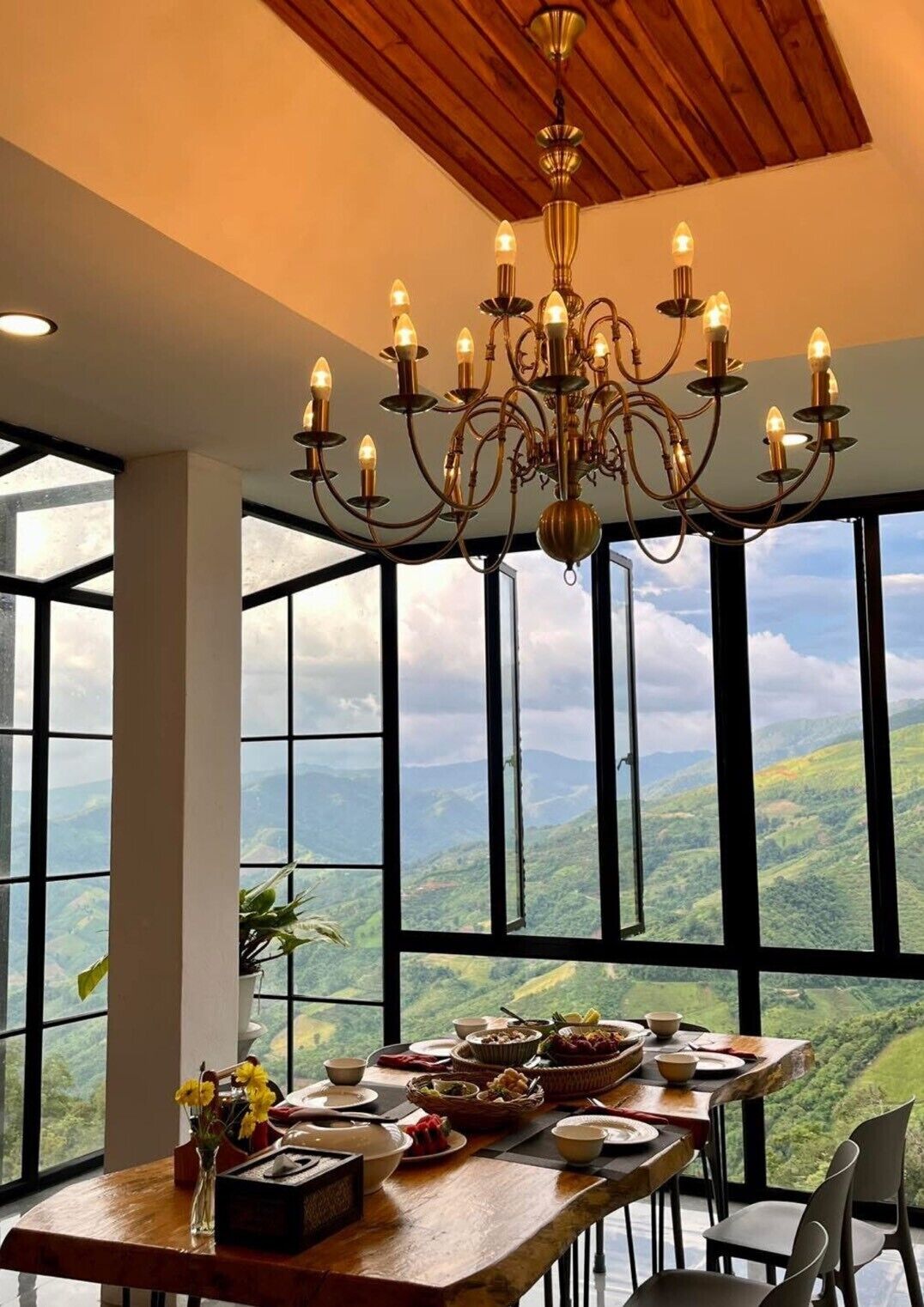 Uma sala de jantar com lustre, janelas amplas e mesa posta para refeição.