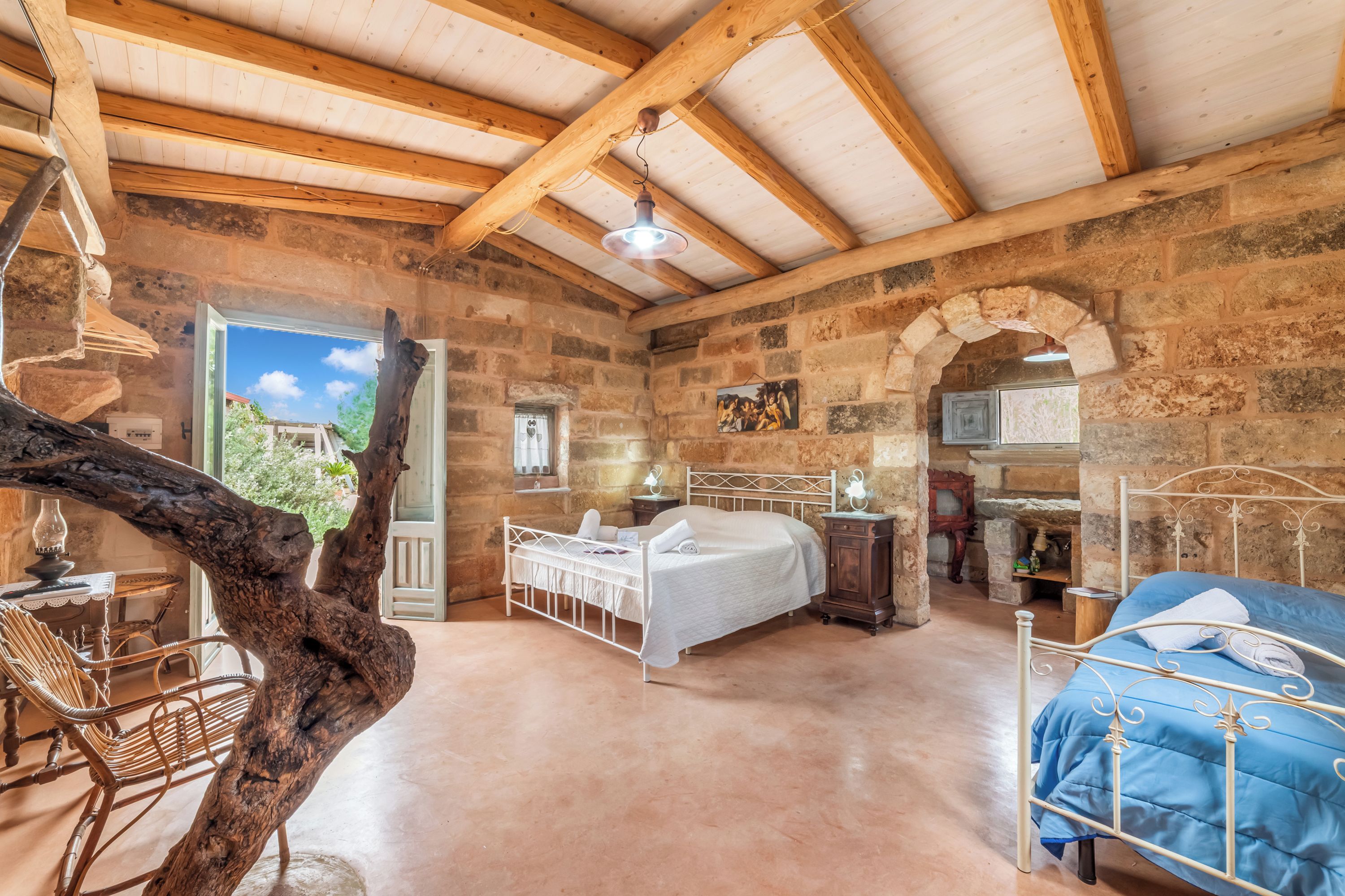Quarto rústico de pedra com uma cama, uma cadeira e teto de madeira.