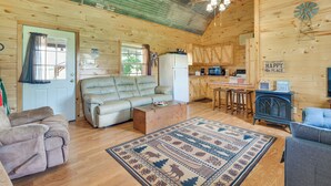 Interior de uma cabana com sala de estar, sofá, mesa de centro, tapete, cozinha e um aviso dizendo 'Esta cabana é o meu refúgio feliz'.
