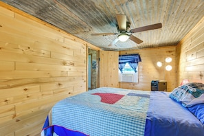 Quarto de cabana de madeira com cama, ventilador de teto e janela com cortinas.