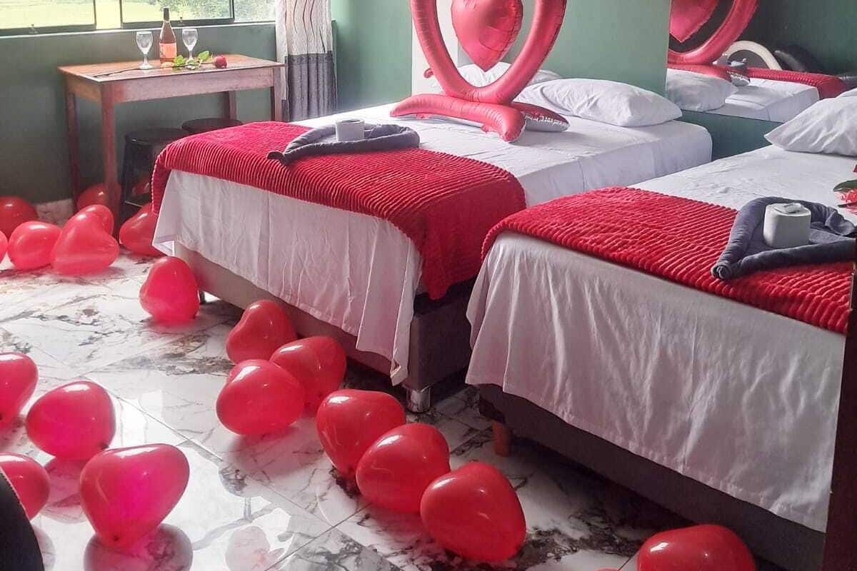 Quarto de hotel com duas camas, uma mesinha com garrafa e copos, e vista para o verde pela janela.
