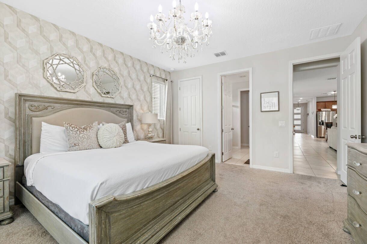 Quarto com uma cama grande, um candelabro e uma porta que dá para um corredor.