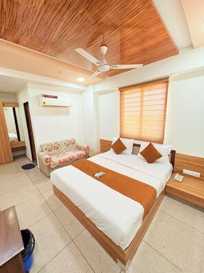 Um quarto com cama, ventilador de teto, janela com persianas, sofá e ar-condicionado fixado na parede.