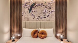 Quarto com cama, duas mesas de cabeceira, luminária fixada na parede e painel decorativo.