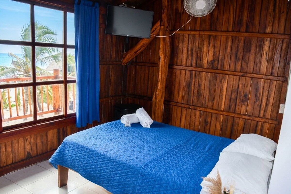 Quarto com cama, televisão e vista para a praia.