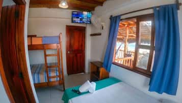 Quarto com cama de solteiro, uma cama individual, televisão, janela com cortinas e vista para a praia.