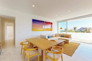Uma sala de estar moderna com uma mesa de jantar de madeira, um sofá e uma grande janela com vista para a cidade.