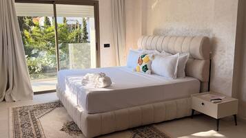 Um quarto moderno com uma cama grande, uma mesa de cabeceira e vista para o verde pela janela.