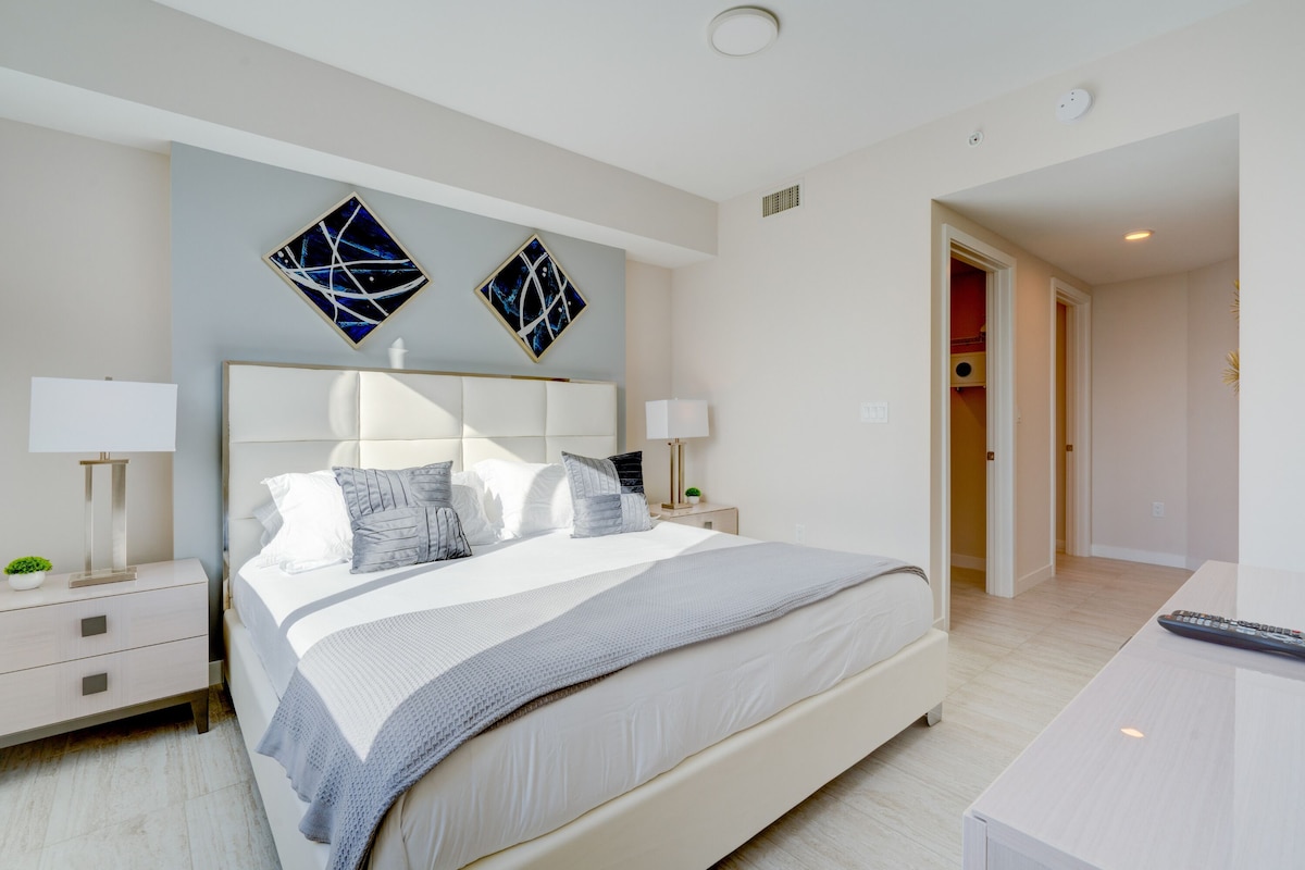 Quarto moderno com uma cama grande, mesas de cabeceira e arte abstrata na parede.