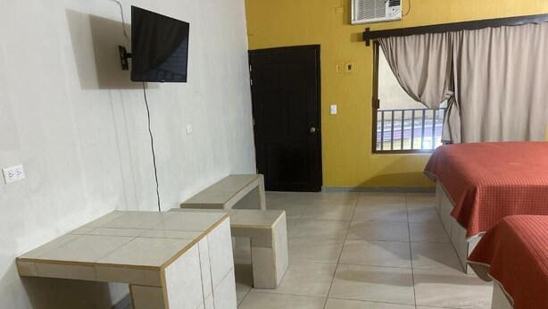 Quarto com cama, televisão na parede, janela com cortinas e chão revestido com azulejos.