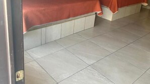 Quarto de hotel com duas camas, piso ladrilhado e porta com puxador.