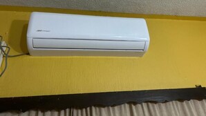 Unidade de ar condicionado branca fixada em uma parede amarela.