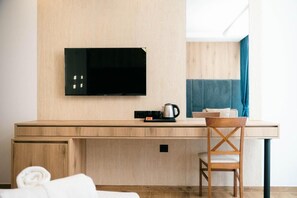 Quarto de hotel moderno com uma escrivaninha de madeira, televisão na parede, uma cadeira e uma cama com uma toalha enrolada.