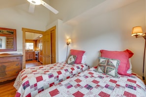 Quarto com duas camas, móveis de madeira, penteadeira e vista para a cozinha através de uma porta aberta.