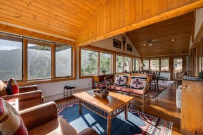 Quarto espaçoso com tetos de madeira e grandes janelas com vista para as montanhas.