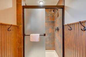 Um chuveiro com porta de vidro, uma toalha pendurada em um suporte e painéis de madeira nas paredes.