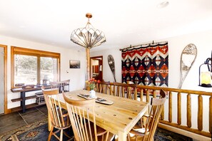 Uma área de refeições com uma mesa e cadeiras de madeira, um candelabro e vista para o exterior.