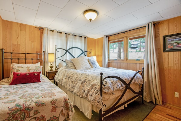 Quarto com duas camas, paredes de madeira, janela com cortinas e luminária no teto.
