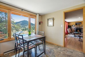 Uma área de refeições com mesa e cadeiras, vista para o exterior e uma lareira ao fundo.