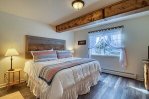 Quarto com cabeceira de madeira, cama grande com várias almofadas, luminária de cabeceira, janela com cortinas e radiador.