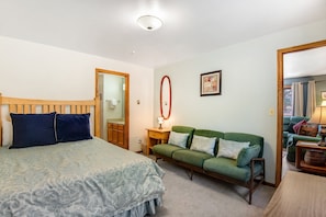 Quarto com cama, sofá verde, mesa de cabeceira de madeira e espelho.