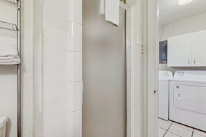 Uma área de lavanderia com máquina de lavar e secadora, um porta-toalhas e uma parede com azulejos brancos.