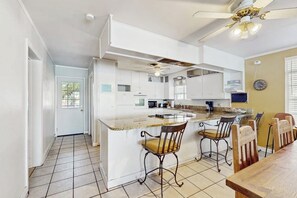 Uma cozinha com ilha central, banquetas, ventilador de teto e mesa de jantar com cadeiras.