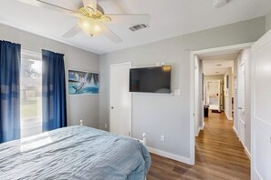 Quarto com cama, ventilador de teto, TV e corredor que dá para outros cômodos.