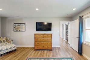 Quarto com cómoda de madeira, sofá, televisão de tela plana e quadro na parede.