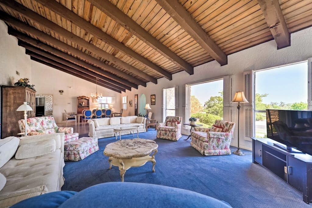 Uma sala de estar ampla com teto de madeira alto, televisão e uma grande janela com vista para o exterior.