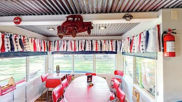 Uma área de refeições com uma mesa e cadeiras vermelhas, um automóvel antigo como decoração e um extintor de incêndio na parede.